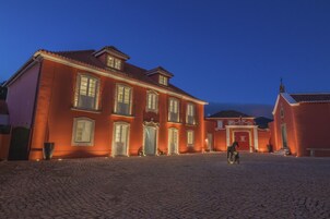 Um edifício histórico com um pátio de paralelepípedos, janelas amplas e uma varanda.