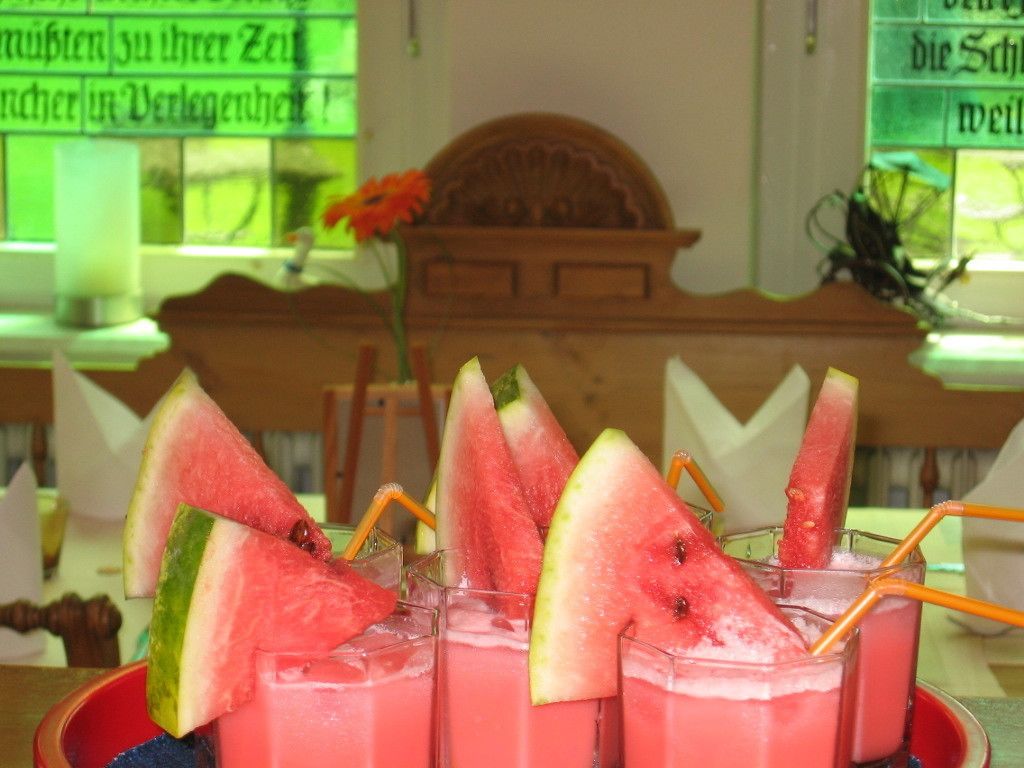 Uma mesa com vários copos de bebida rosa, cada um decorado com uma fatia de melancia e um canudo de laranja.