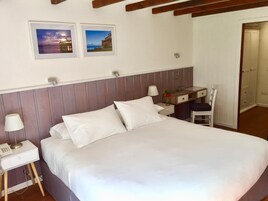 Quarto com uma cama grande, uma escrivaninha, uma cadeira e duas fotos emolduradas na parede.