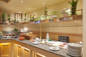 Uma mesa de buffet com diversos alimentos, uma placa de sinalização e plantas decorativas.