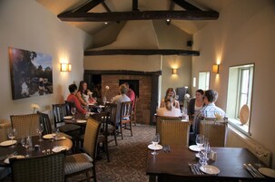 Um restaurante com vigas de madeira, lareira de tijolos e mesas com cadeiras.