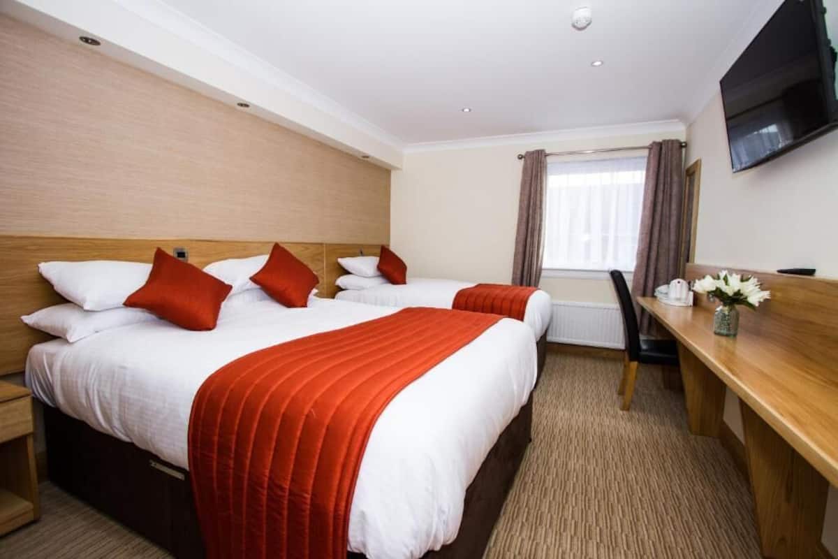 Quarto de hotel com duas camas, uma escrivaninha de madeira, televisão e janela com cortinas.