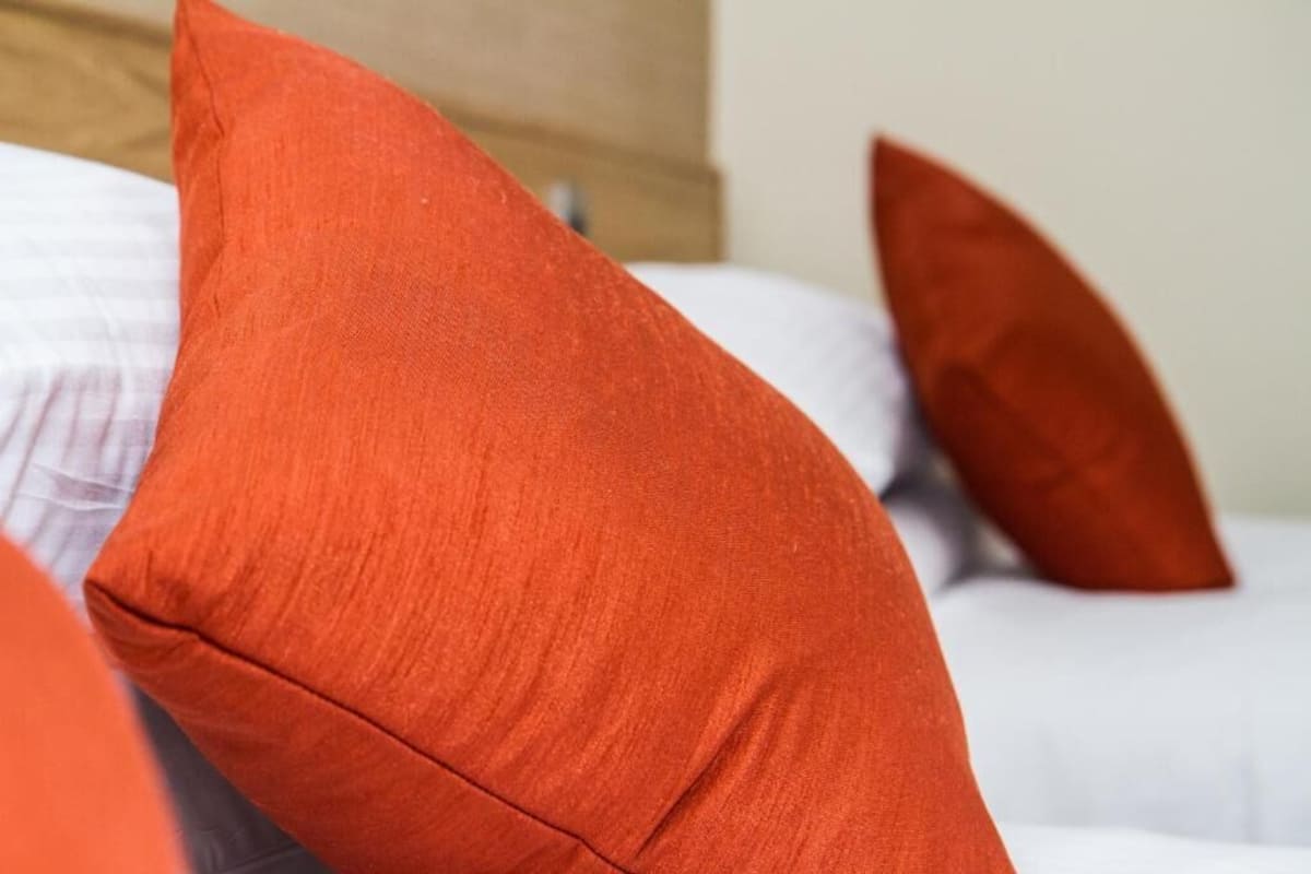 Um close-up de uma cama com roupa de cama branca e vários travesseiros laranja.