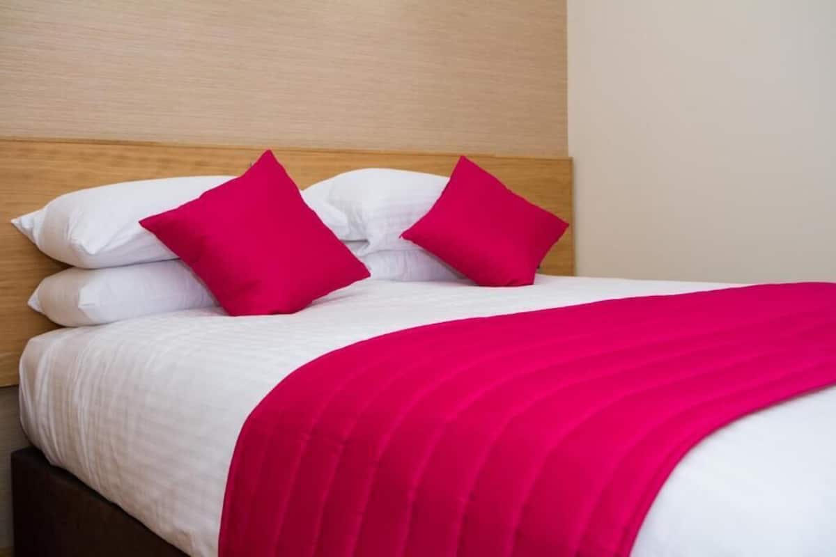 Cama com roupa de cama branca e duas almofadas rosa vibrante.