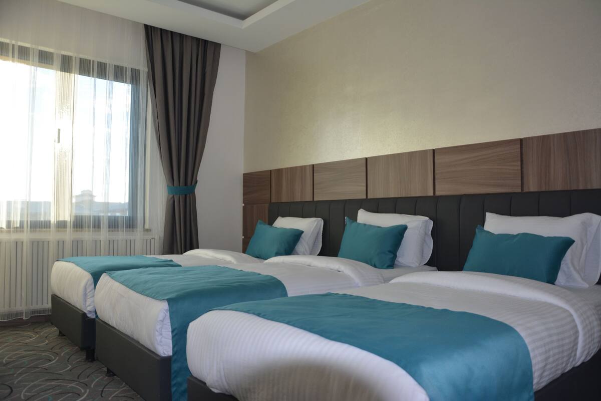 Quarto de hotel com duas camas, uma janela grande com cortinas e vista para a cidade.
