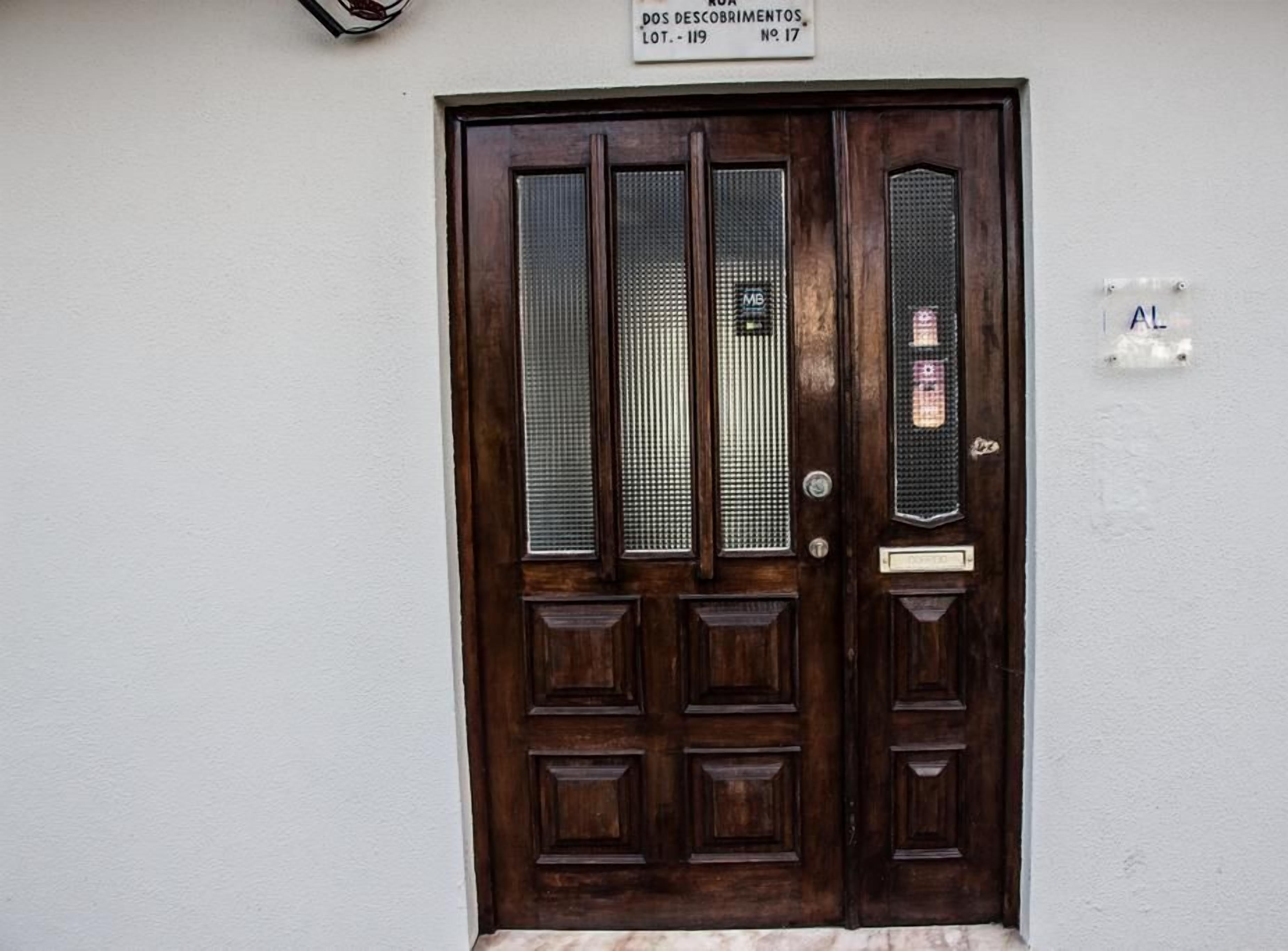 Uma porta de madeira escura com uma placa acima, uma abertura para correspondência e uma pequena caixa de correio na parede.