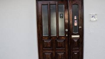 Uma porta de madeira escura com uma placa acima, uma abertura para correspondência e uma pequena caixa de correio na parede.