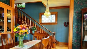 Uma área de refeições com mesa de madeira, cadeiras, um vaso de flores, uma escada e um lustre.