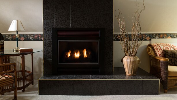 Uma lareira com design moderno, uma mesa de vidro com uma luminária e uma cadeira de vime.
