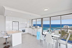 Cozinha moderna com uma ilha grande, armários brancos e vista para o oceano.