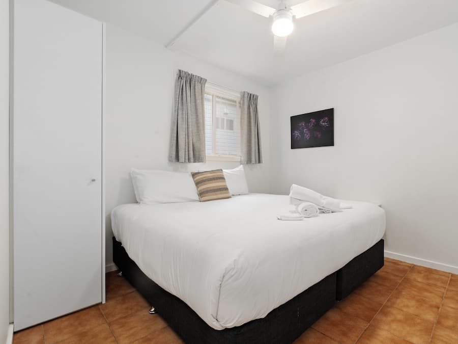 Quarto com cama, janela com cortinas, ventilador de teto e uma obra de arte pendurada na parede.