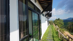 Um edifício moderno com grandes janelas de vidro, um deck de madeira e um caminho de pedra que leva a uma paisagem verdejante.
