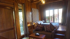Quarto com decoração em madeira, uma cama, um sofá, uma mesa de centro e uma janela com cortinas.