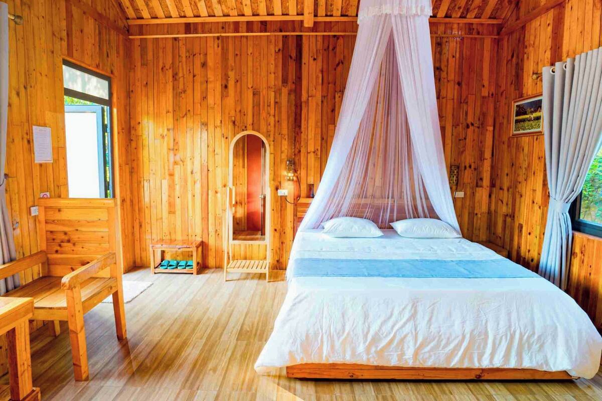 Quarto de cabana de madeira com cama, um banco e uma pequena mesa com garrafas.