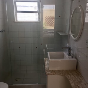 Um banheiro com chuveiro em cabine de vidro, pia com espelho e paredes revestidas com azulejos.