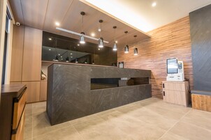 Uma área de recepção moderna com balcão de mármore, painéis de madeira e um quiosque de autoatendimento.