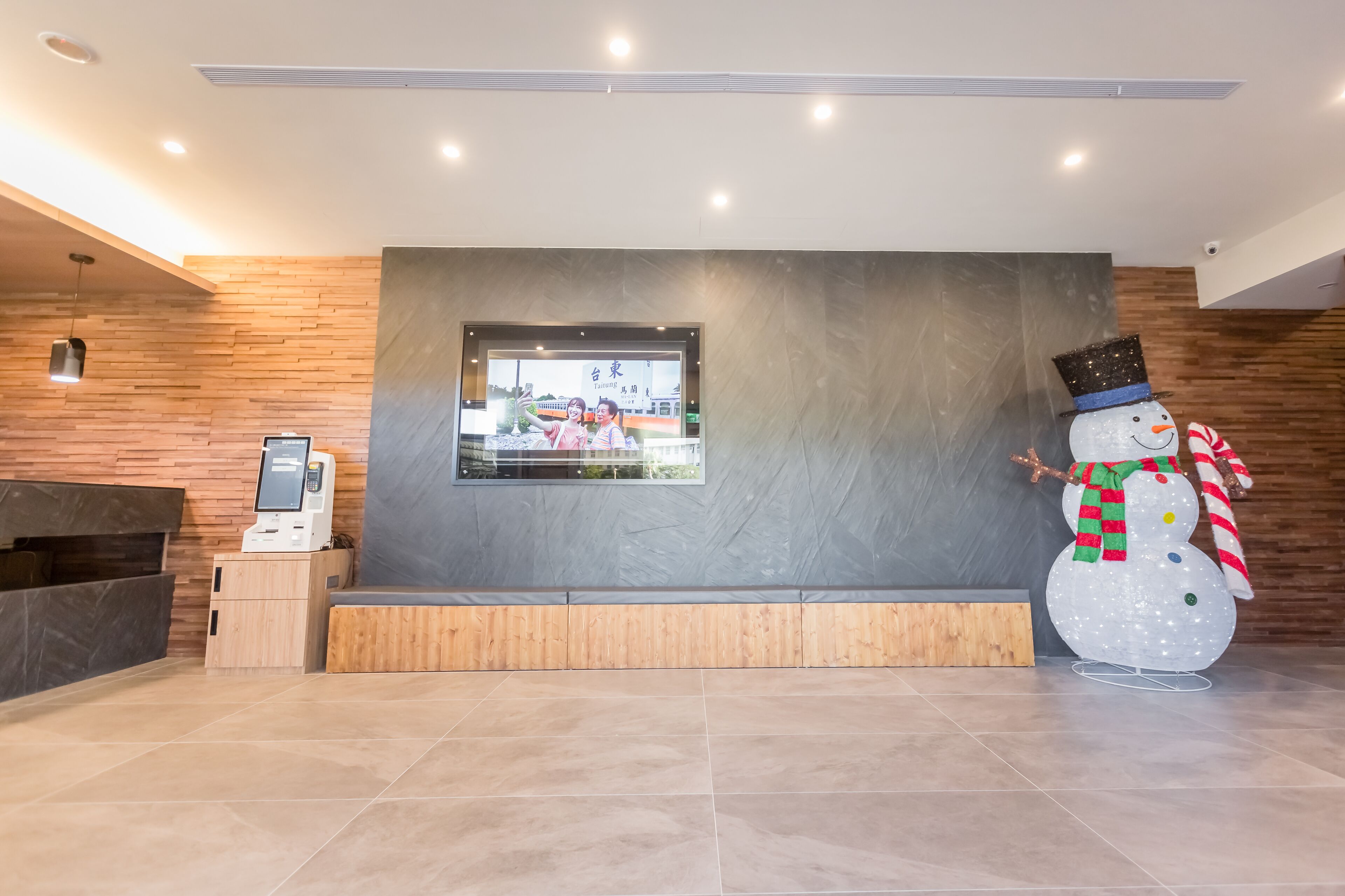 Uma área de recepção com um quiosque digital, uma tela grande exibindo uma vista panorâmica e uma decoração de boneco de neve.