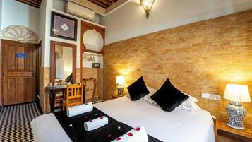 Quarto de hotel com uma cama grande, uma escrivaninha de madeira, uma cadeira, um espelho, parede de tijolos e um lustre.
