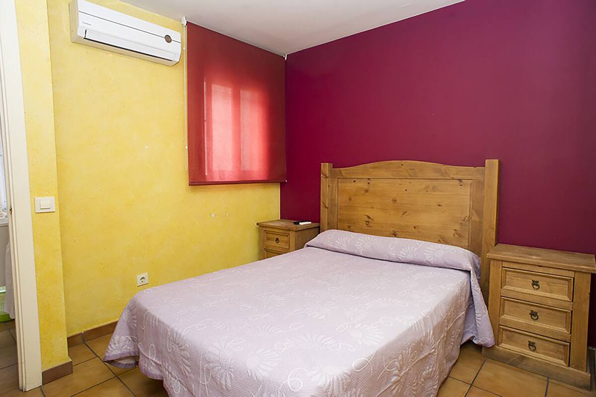Quarto com cama de madeira, parede vermelha e parede amarela.