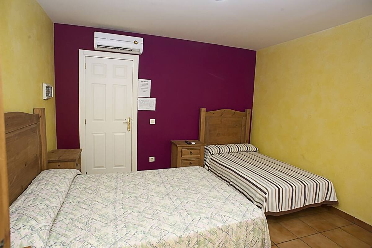 Quarto com duas camas, cabeceira de madeira, porta branca e ar condicionado.