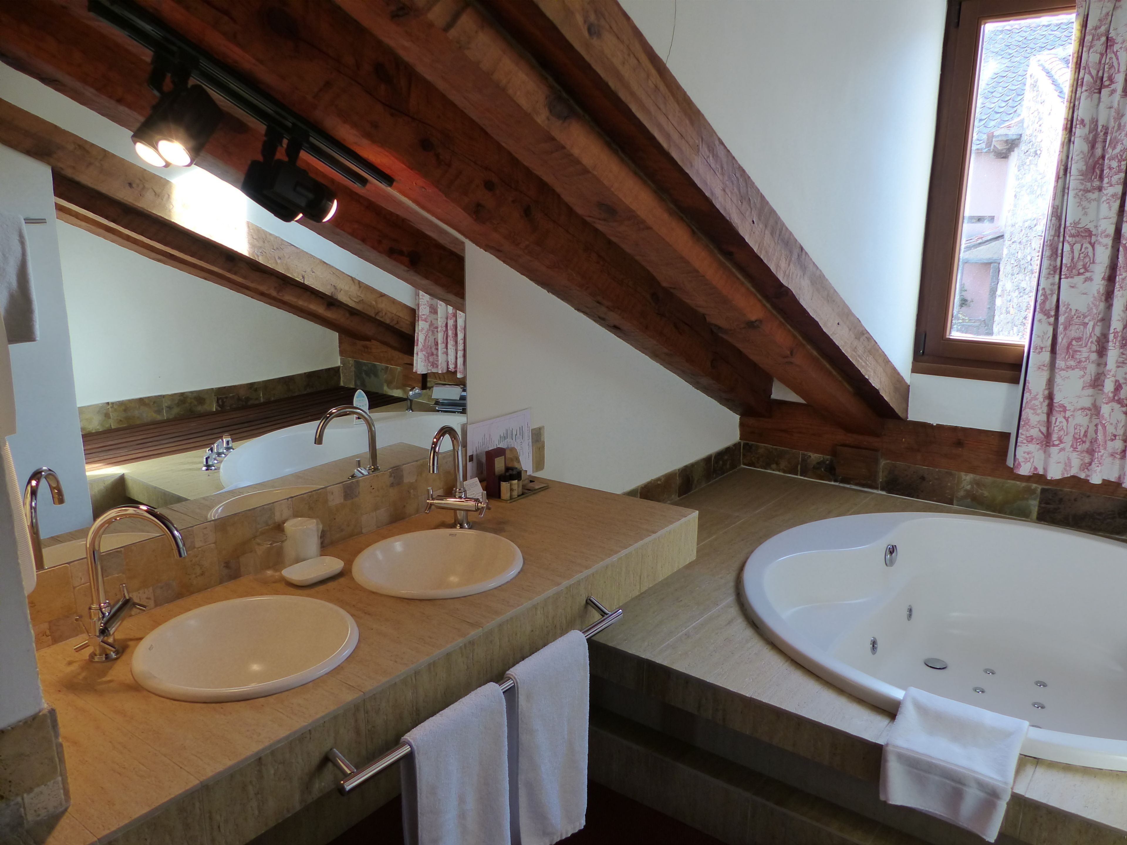 Casa de banho com duas pias, uma banheira, vigas de madeira, uma janela e um espelho.
