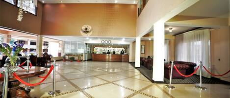 Um hall de hotel com balcão de recepção, área de estar e teto decorativo.