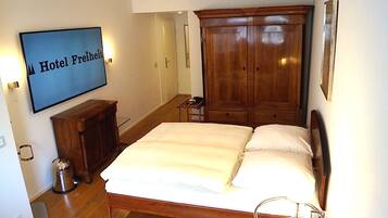 Quarto de hotel com cama, guarda-roupa de madeira, televisão e máquina de café.
