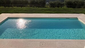 Uma piscina retangular com água azul cristalina, rodeada por um deck ladrilhado.