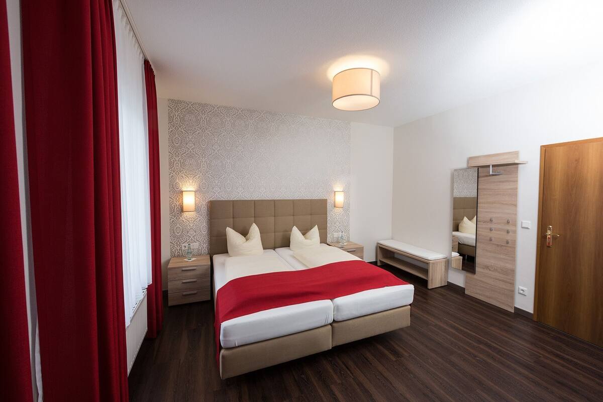 Quarto de hotel com cama, mesas de cabeceira, espelho e guarda-roupa.