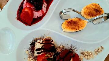 Um prato branco com três sobremesas: uma sobremesa de morango com calda de frutas vermelhas, uma sobremesa coberta de chocolate com morango e um pedaço de bolo com um garfo.