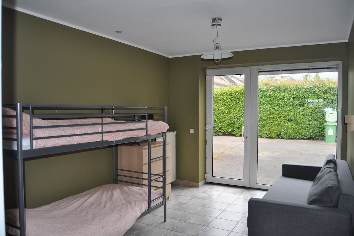 Um quarto de dormitório com beliches, um sofá e uma porta de vidro deslizante que dá para uma área externa.