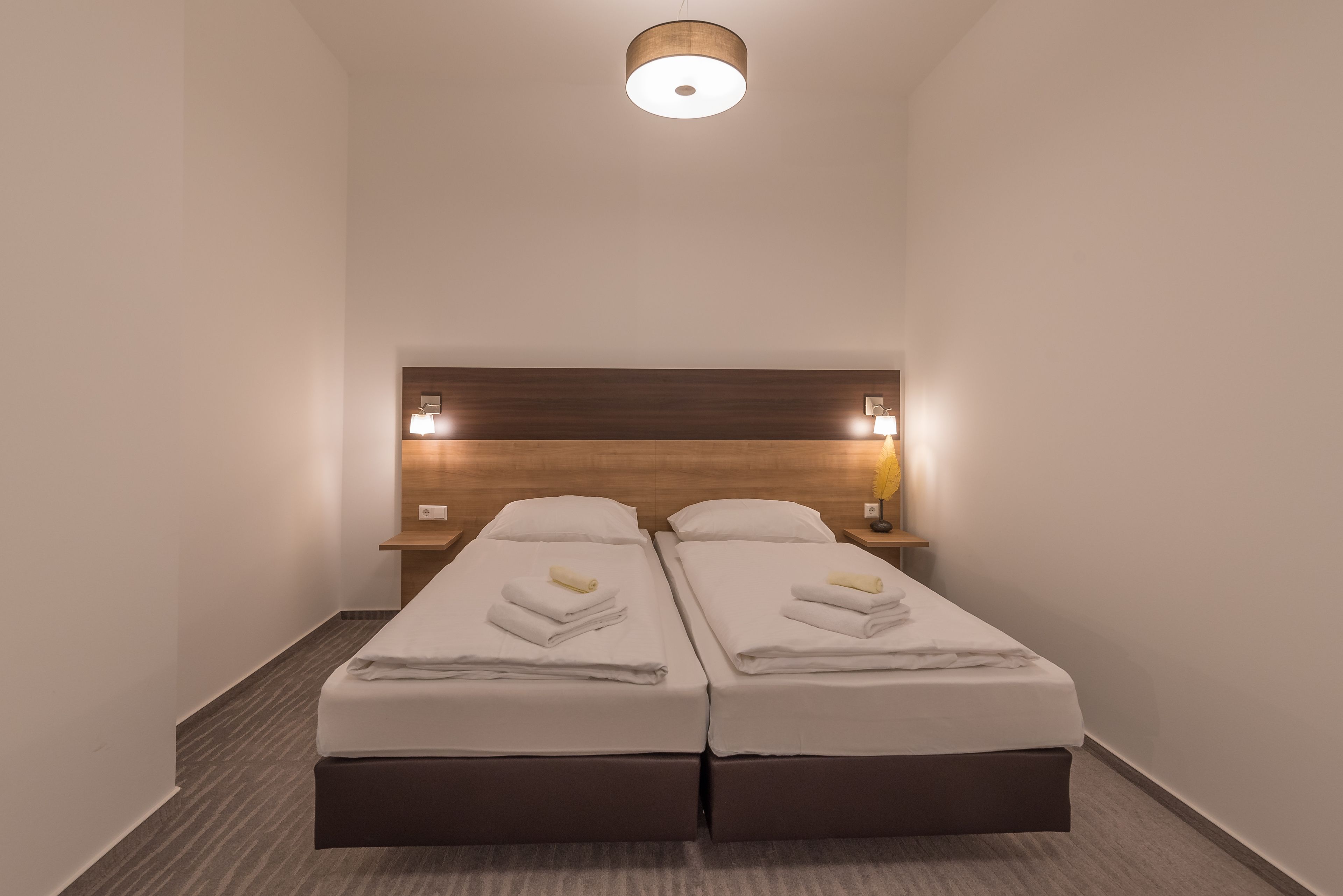 Quarto duplo com duas camas, cabeceira de madeira, abajures e uma mesinha de cabeceira.