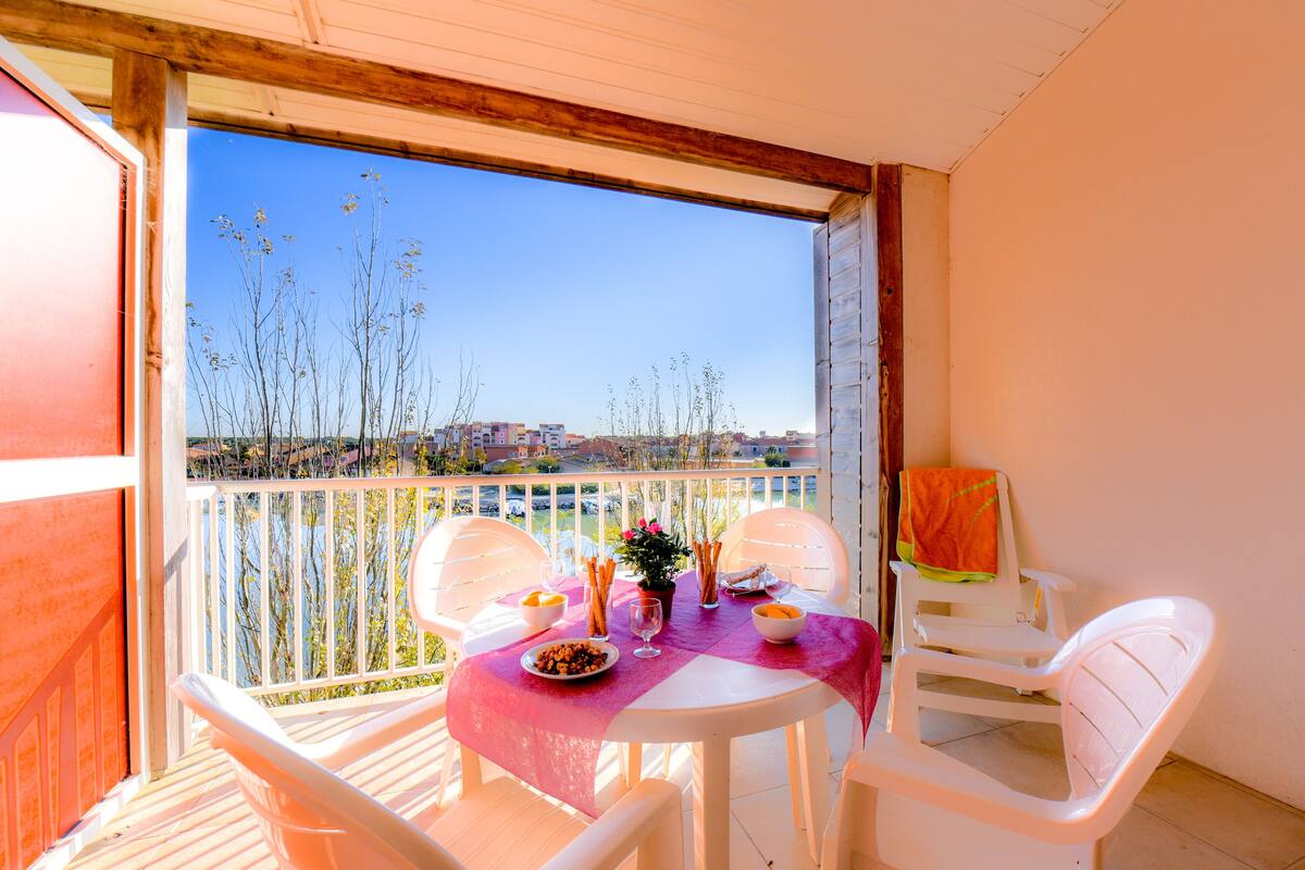 Varanda com mesa posta para dois, cadeiras, planta em vaso e vista para a paisagem.
