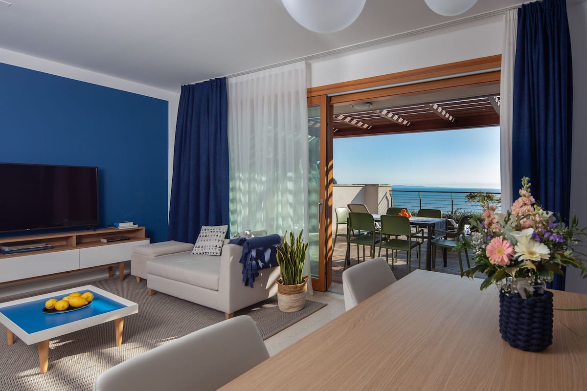 Uma sala de estar moderna com um sofá, uma mesa de centro com limões, uma televisão e um espaço de jantar com mesa e cadeiras.