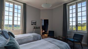 Quarto de hotel com duas camas, uma cadeira, uma mesinha e vista para o exterior.