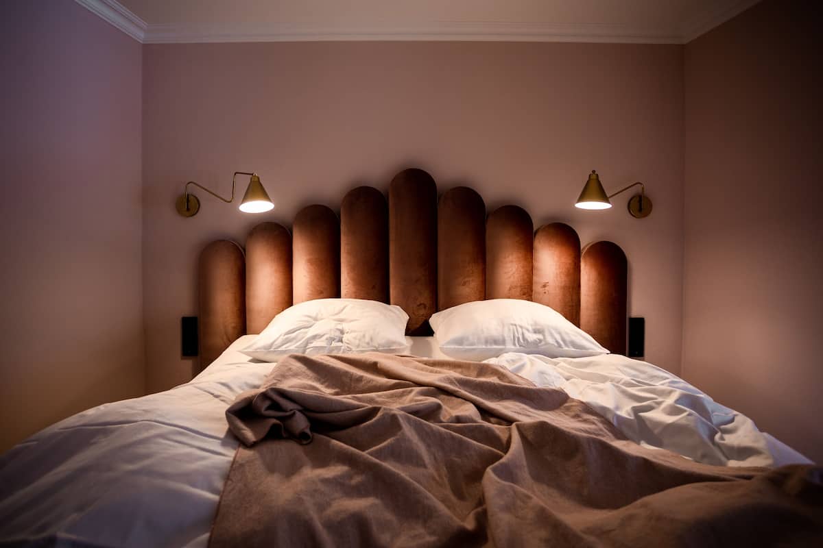 Uma cama com cabeceira de madeira e duas luminárias fixadas na parede.