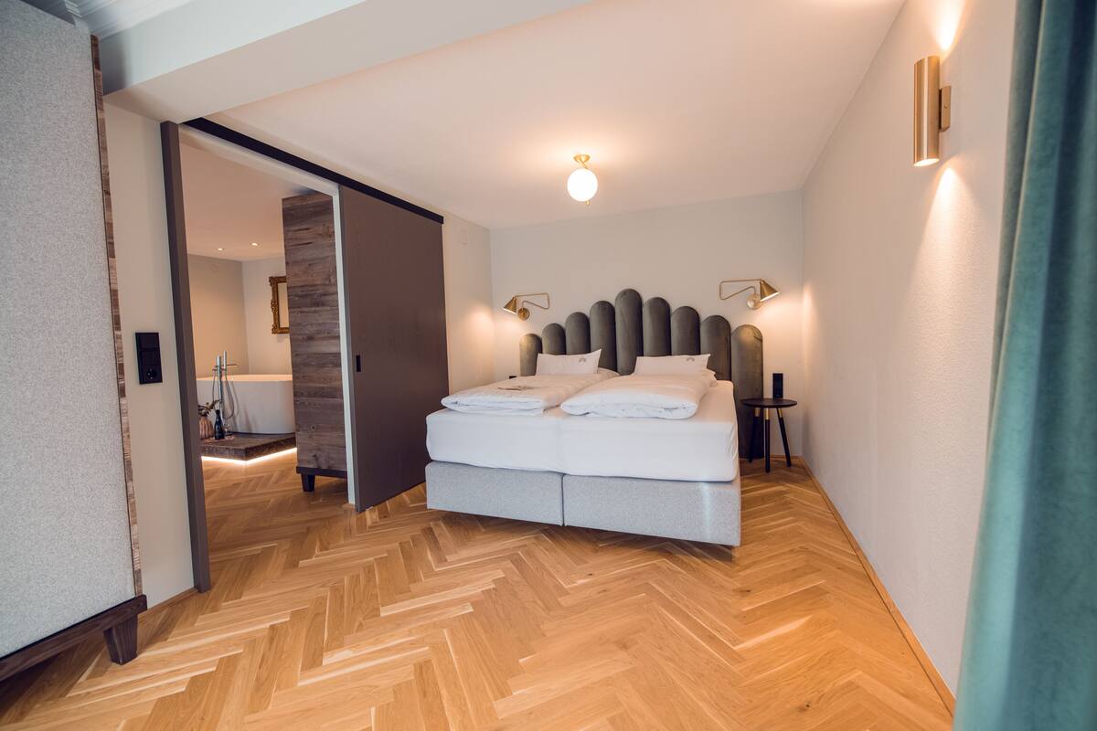 Um quarto moderno com uma cama grande, piso de madeira e uma porta deslizante para outro espaço.