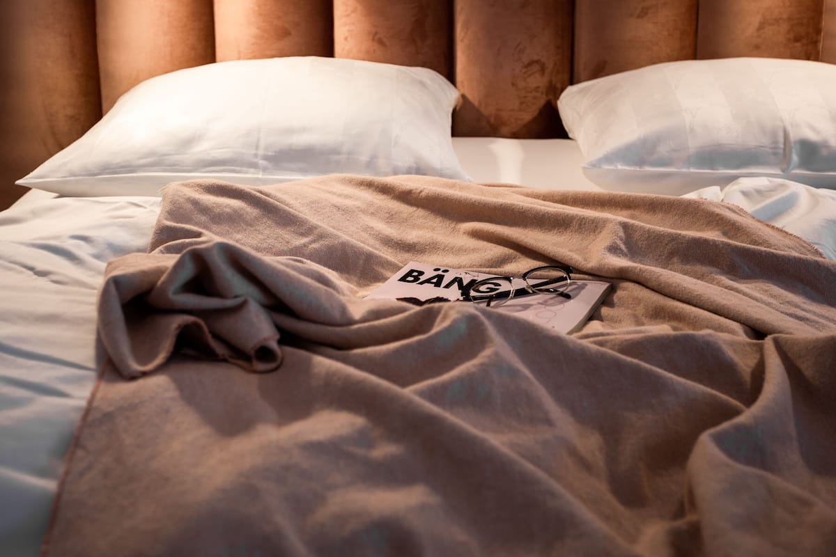 Uma cama com um cobertor marrom, travesseiros brancos e um livro intitulado "BANG".