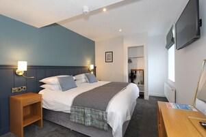 Quarto de hotel com cama, mesa de cabeceira, abajur e televisão de tela plana na parede.