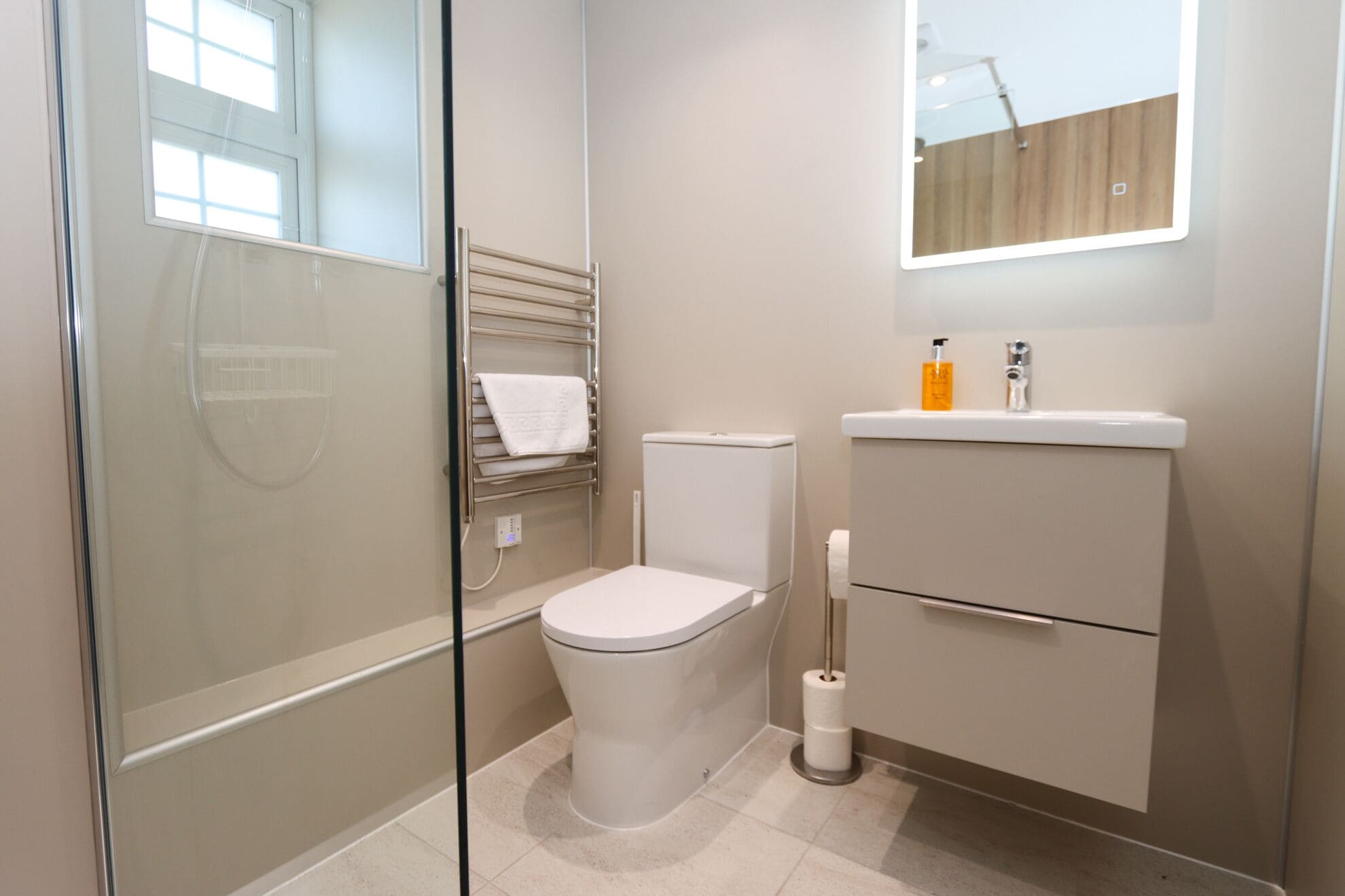 Um banheiro moderno com box de vidro, vaso sanitário, pia com espelho e porta-toalhas.