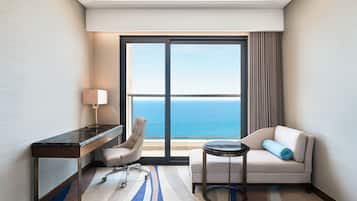 Quarto de hotel com escrivaninha, cadeira, sofá e vista para o mar.