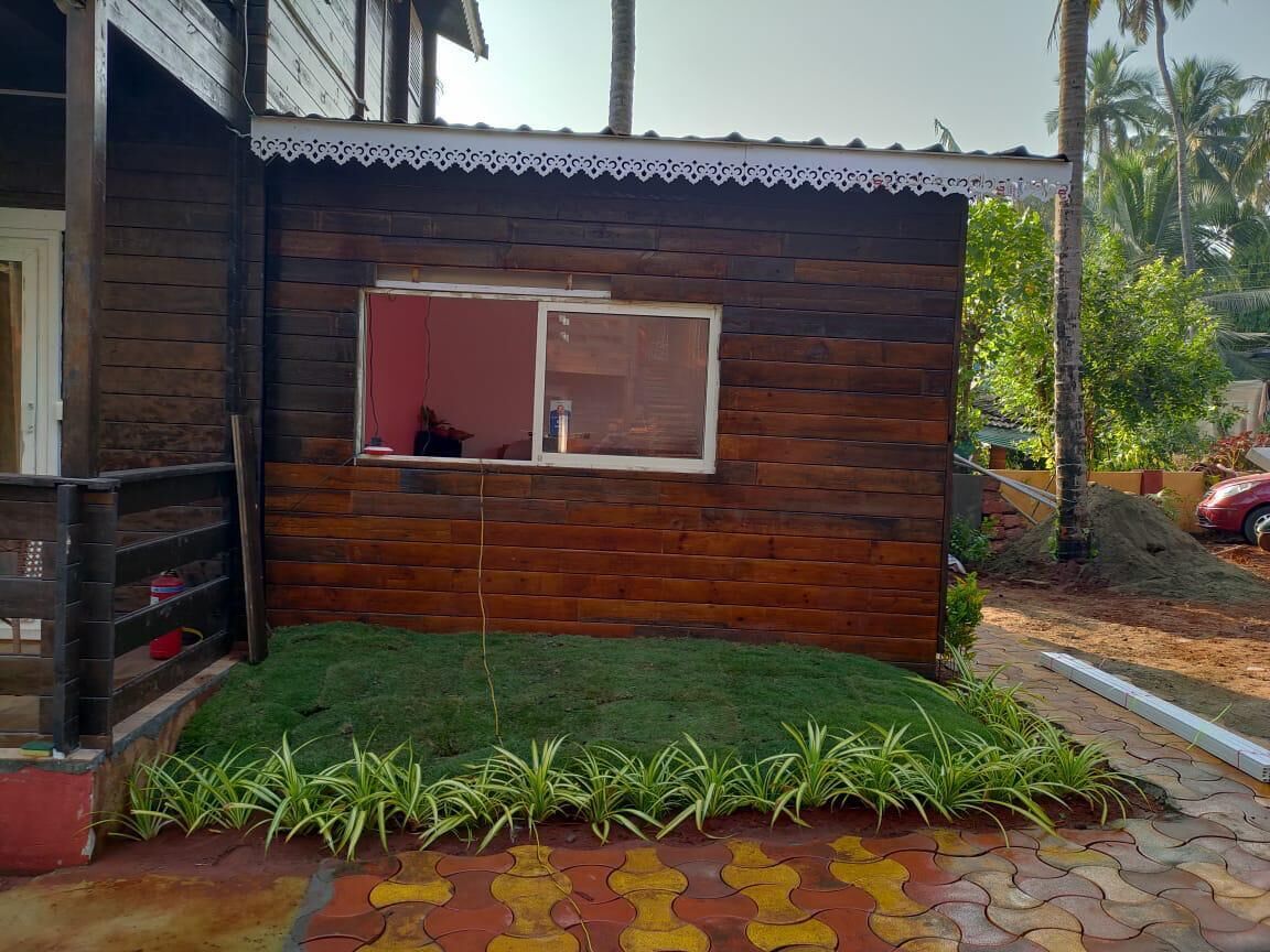 Uma cabana de madeira com janela, uma pequena área gramada e um caminho pavimentado.