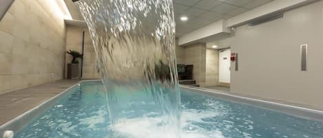 Piscina com cascata, paredes revestidas de azulejos e teto com iluminação embutida.