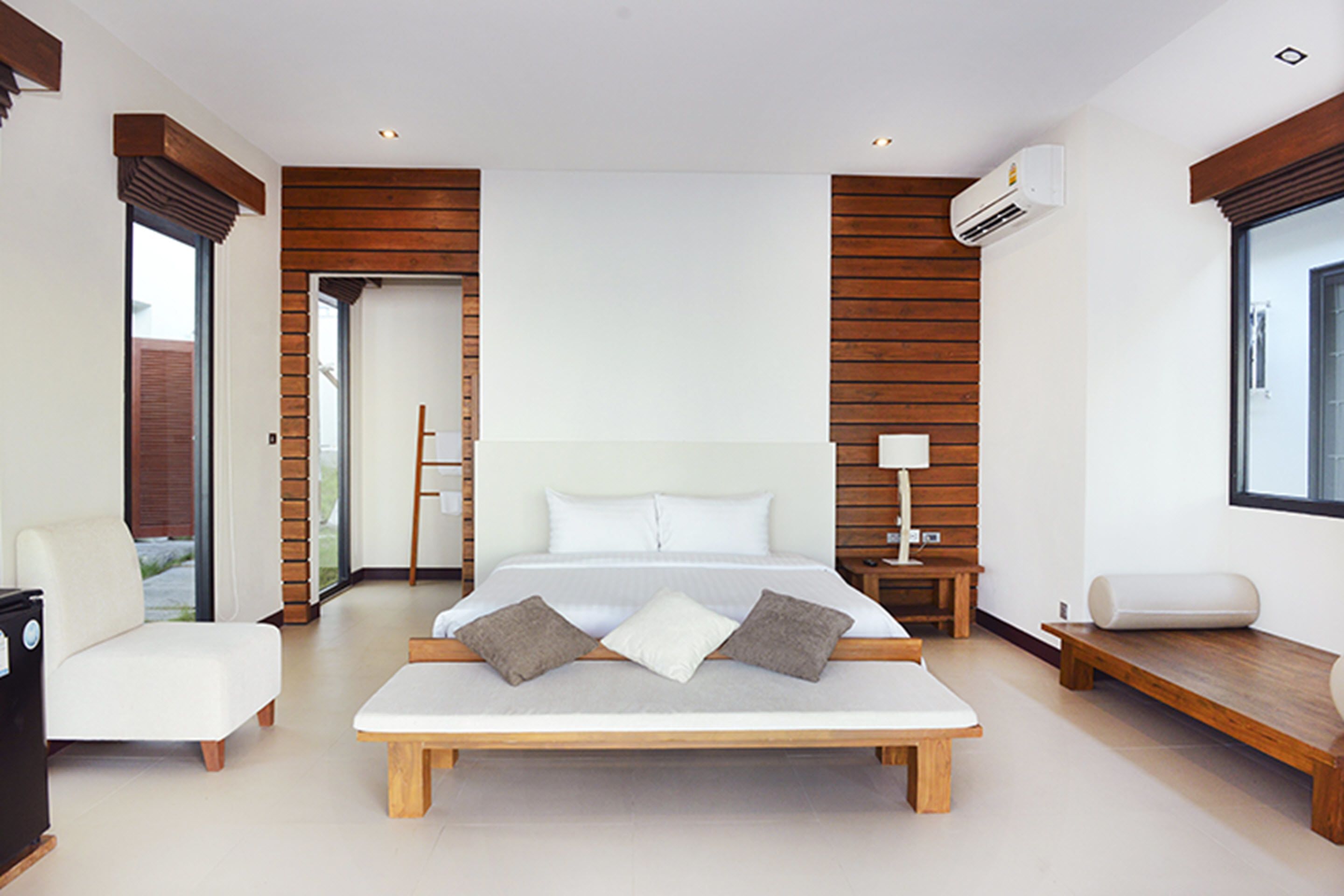 Quarto moderno com uma cama grande, uma mesinha de cabeceira, um banquinho e um sofá.