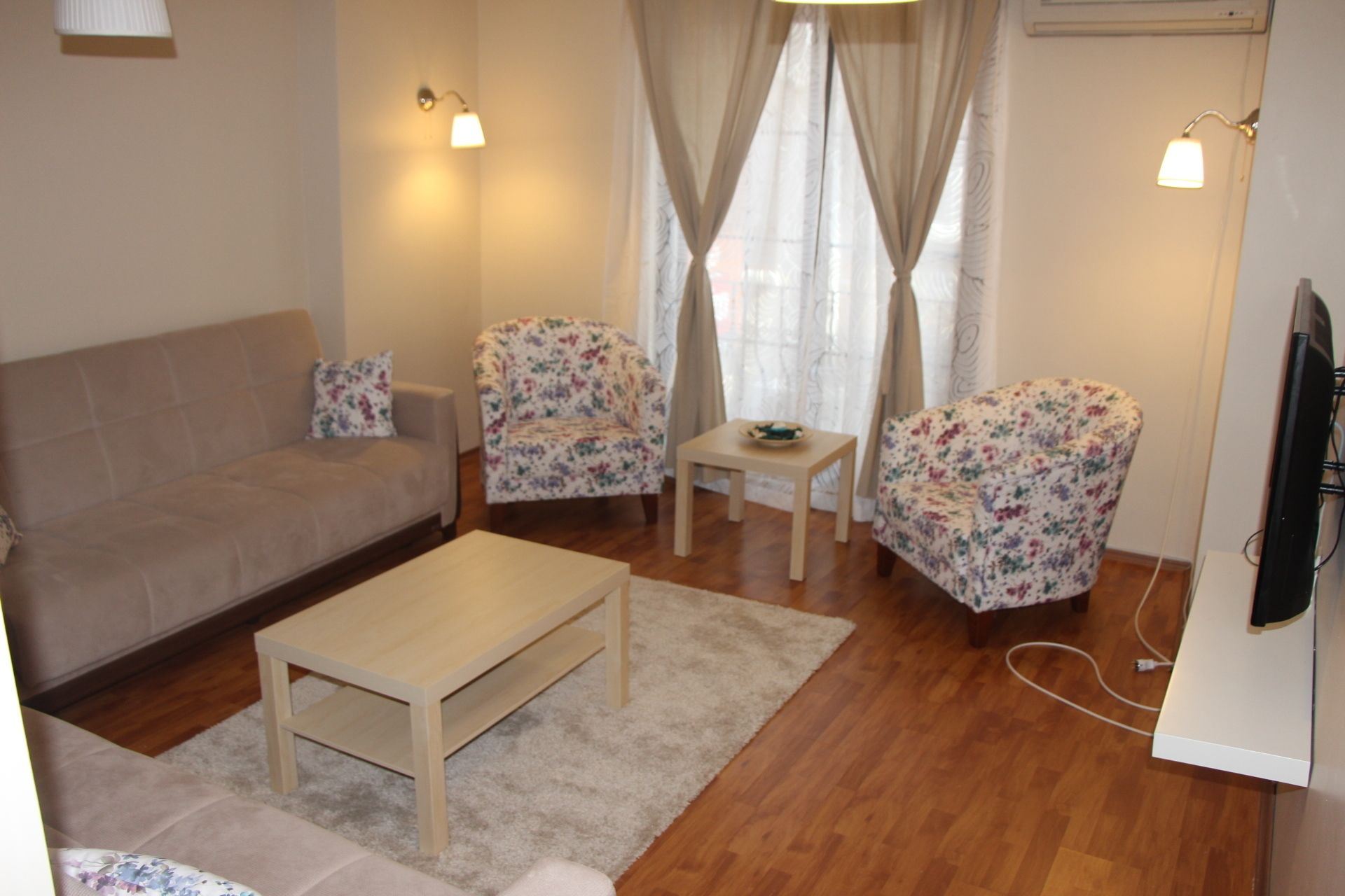 Uma sala de estar com sofá, duas poltronas florais, uma mesinha e uma televisão.