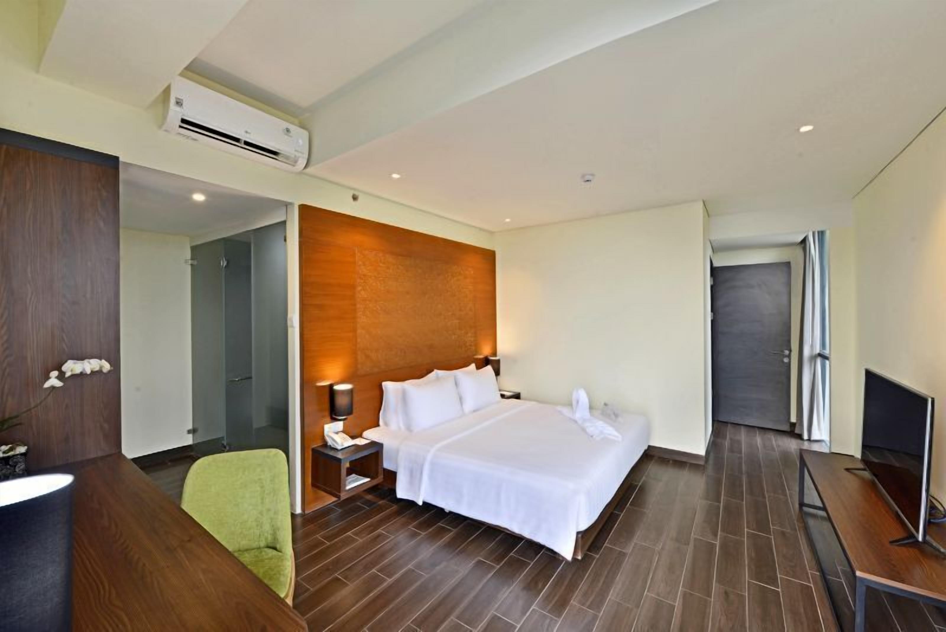 Quarto de hotel moderno com uma cama grande, uma escrivaninha, uma cadeira, uma TV e um ar condicionado.