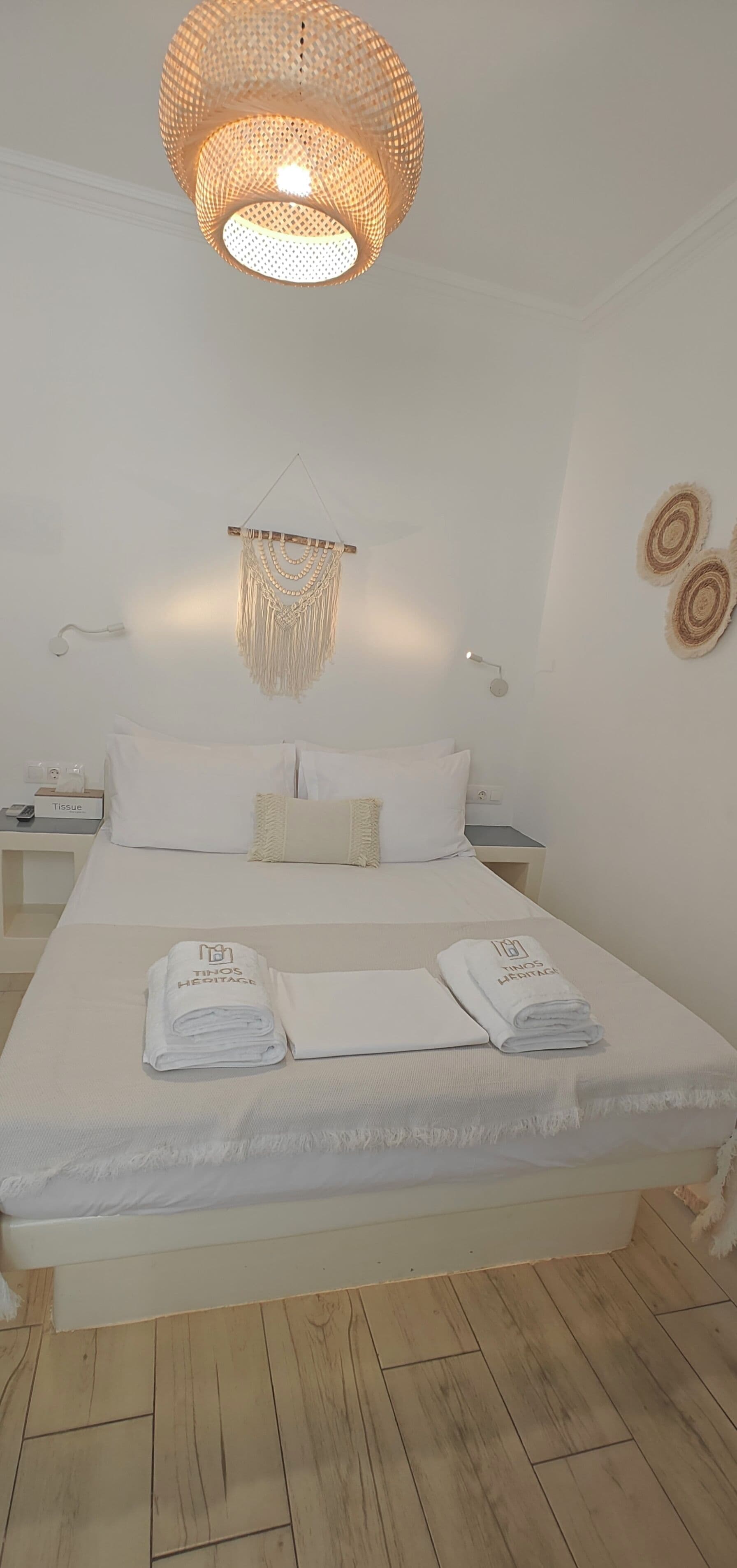 Cama bem arrumada com toalhas, uma decoração de parede em macramé e um luminário tecido acima.