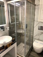 Uma casa de banho moderna com cabine de duche em vidro, lavatório branco e sanita.
