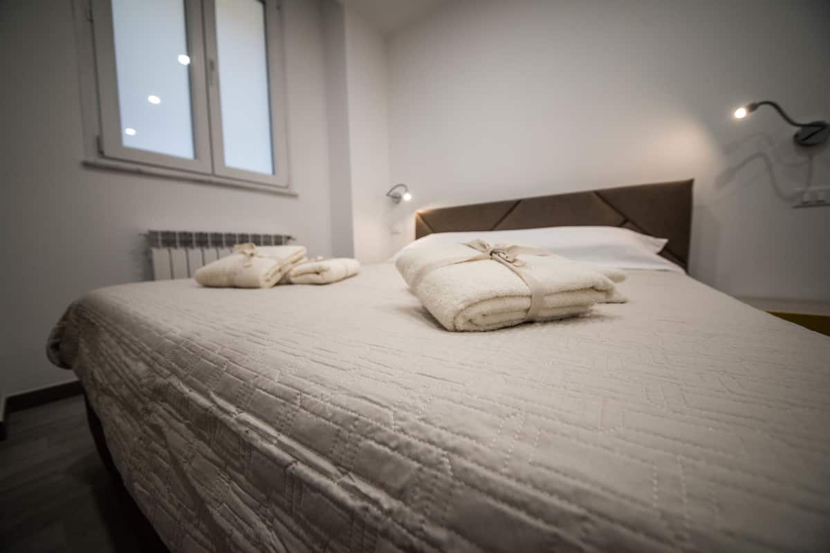 Uma cama bem arrumada com um edredom acolchoado e duas toalhas enroladas ao lado.