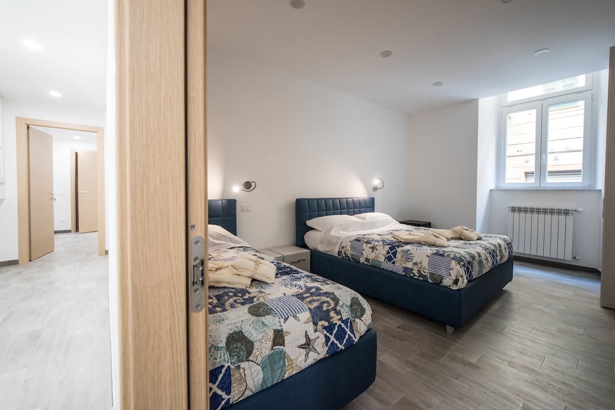 Quarto moderno com duas camas, uma porta de madeira e uma janela com persianas.